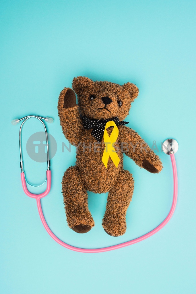 Top view of yellow ribbon on brown teddy bear near stethoscope on blue ...