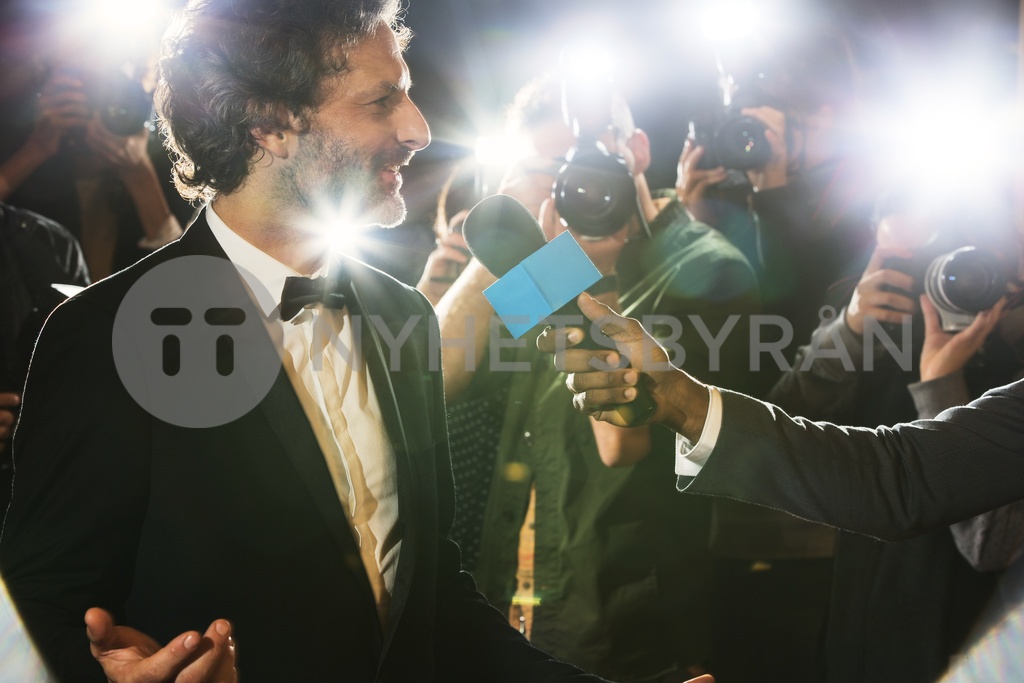 Celebrity being interviewed and photographed by paparazzi at event