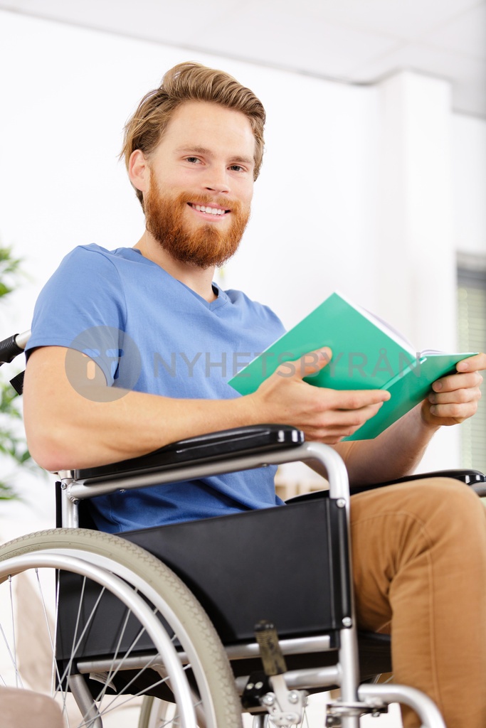 smiling physically handicapped man on wheelchair with books and pencil